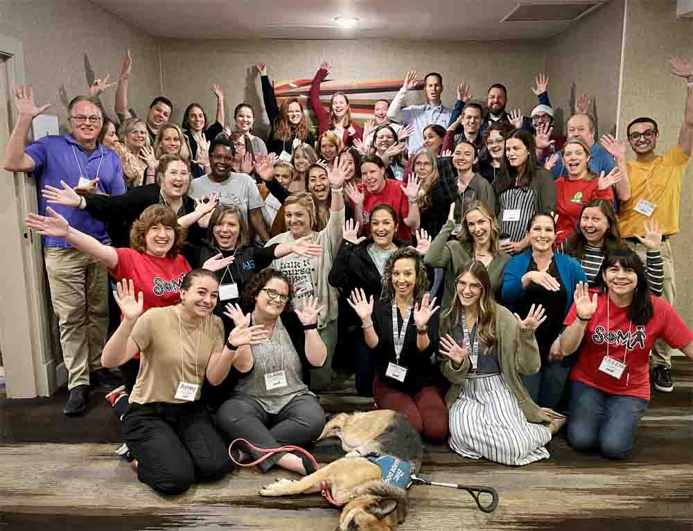 picture shows about 50 people, posing together, smiling and waving.