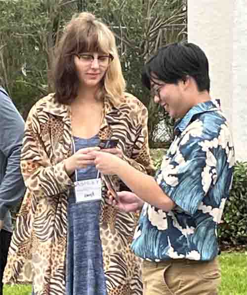 Ashley and Kris are outside on the grass, looking at something that one ...