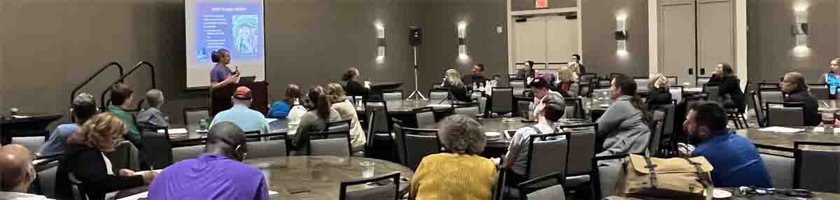 Picture shows about 50 participants in a large room with round tables ...
