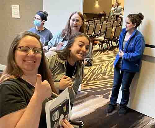 Jessica and Ashley are sitting in the hall, leaning forward holding ...