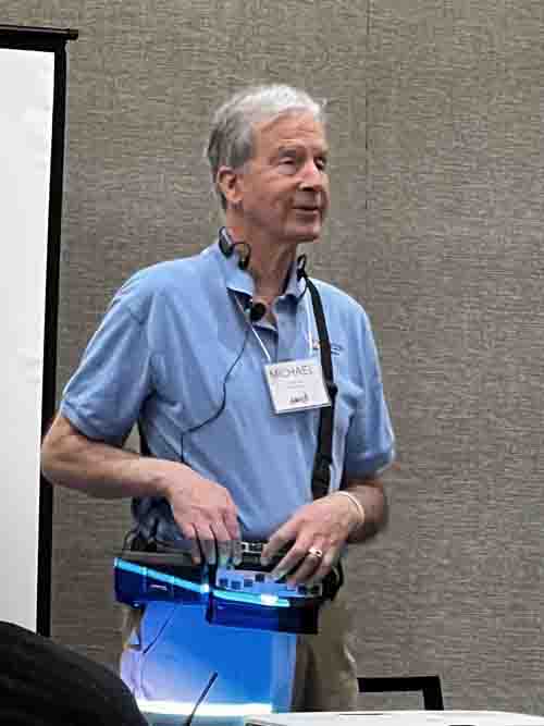 Picture shows Mike May smiling as he stands and talks, reaching into a ...