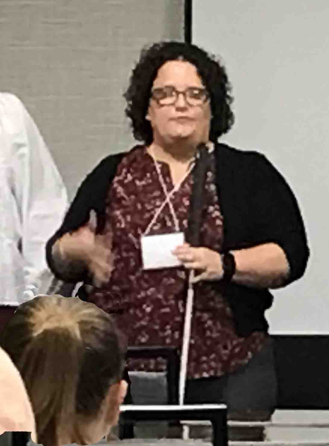 picture shows Elaine holding her cane and speaking to the audience