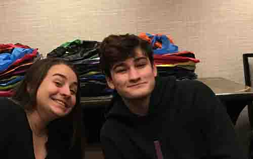 Ashley and Ethan are sitting at the work table, leaning toward each ...